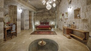 Quarto com paredes de pedra, uma cama, uma escrivaninha e um espelho.