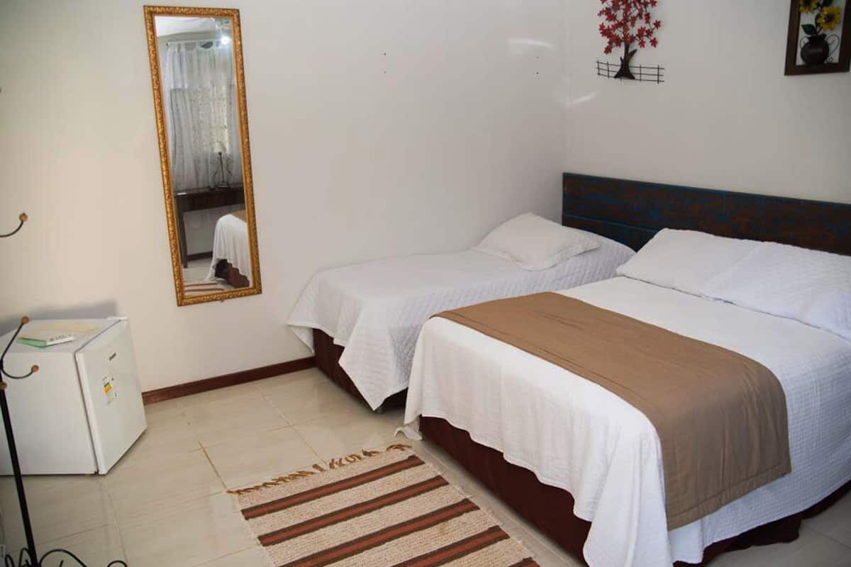 Quarto com duas camas, um espelho, cômoda e tapete.