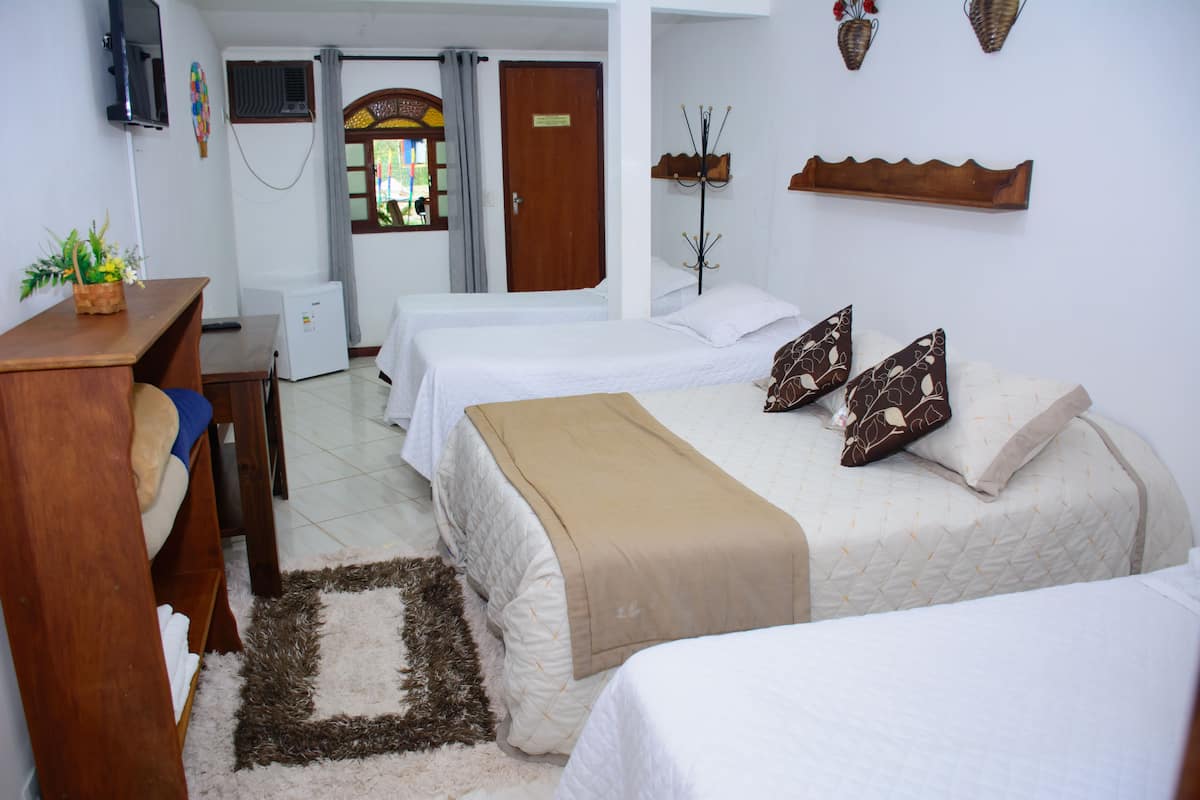 Quarto de hotel com duas camas, uma escrivaninha, uma cadeira, um mini-refrigerador, televisão e janela com cortinas.