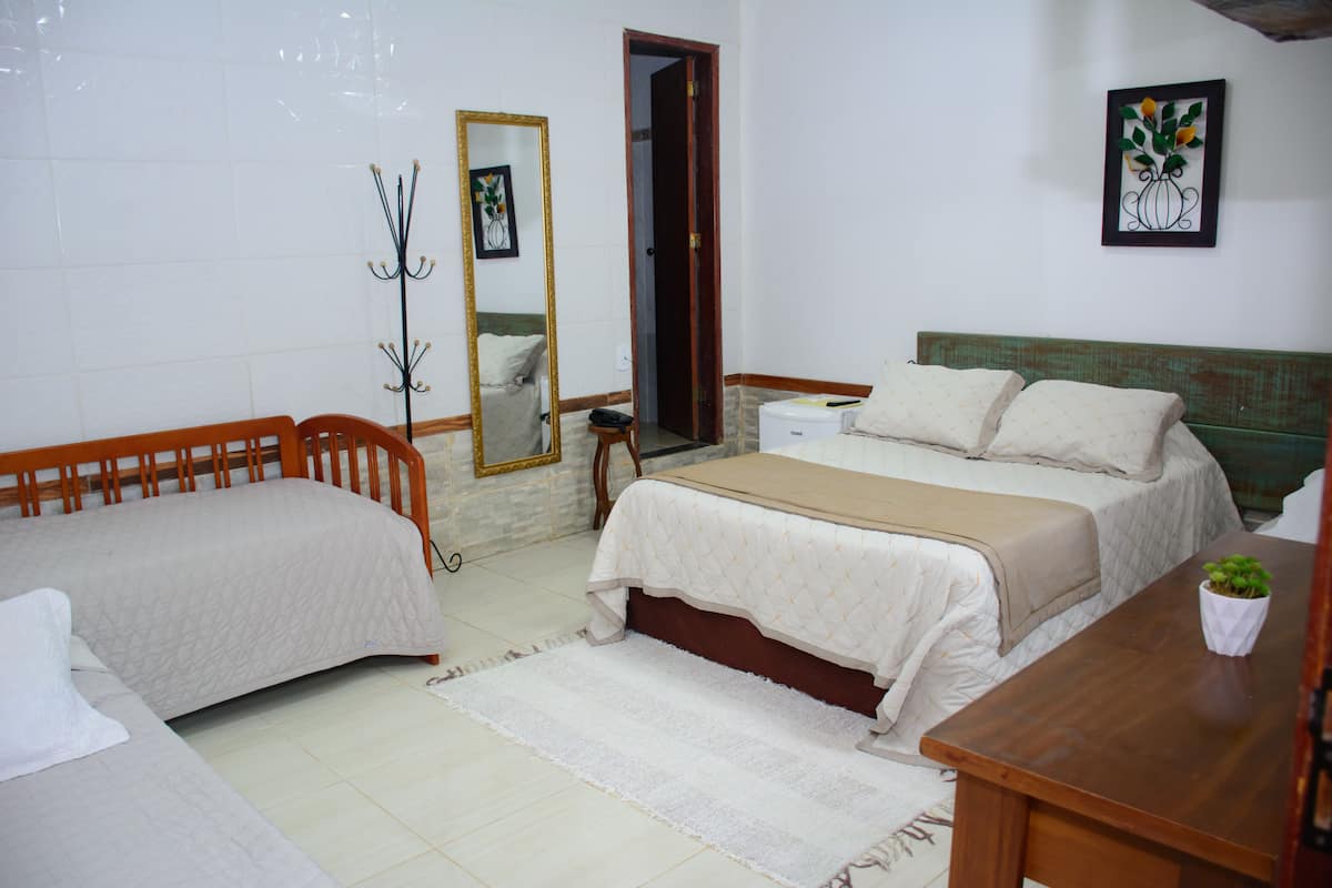 Quarto com duas camas de solteiro, uma mesinha de cabeceira de madeira, um espelho e um quadro pendurado na parede.