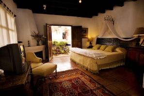 Quarto com cama, uma cadeira, televisão e lareira.