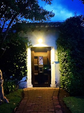 Um caminho leva a um edifício com entrada iluminada, cercado por vegetação.