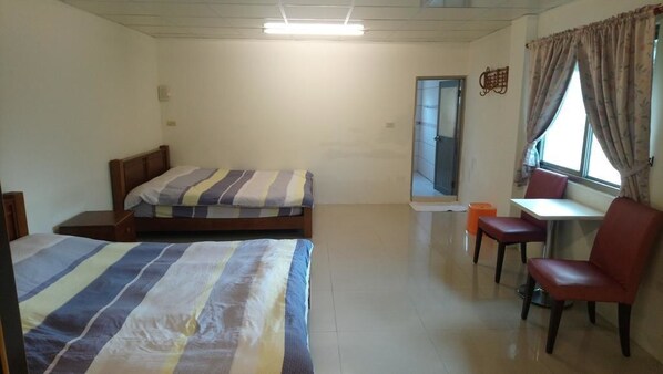 Quarto com duas camas, uma mesa pequena, uma cadeira e uma janela com cortinas.
