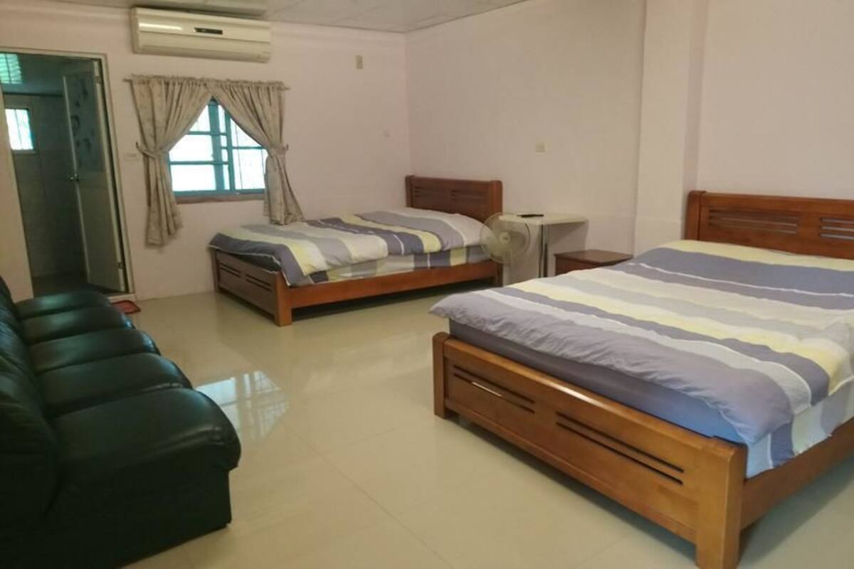 Quarto com duas camas de madeira, um sofá de couro preto, uma mesinha e um ar condicionado.