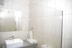 Casa de banho com lavatório branco, espelho e chuveiro.