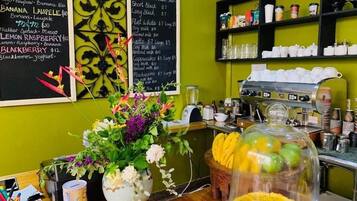 Balcão de café com um quadro de menu, um registrador de caixa e uma exposição de bananas e uma tigela de frutas tampada.