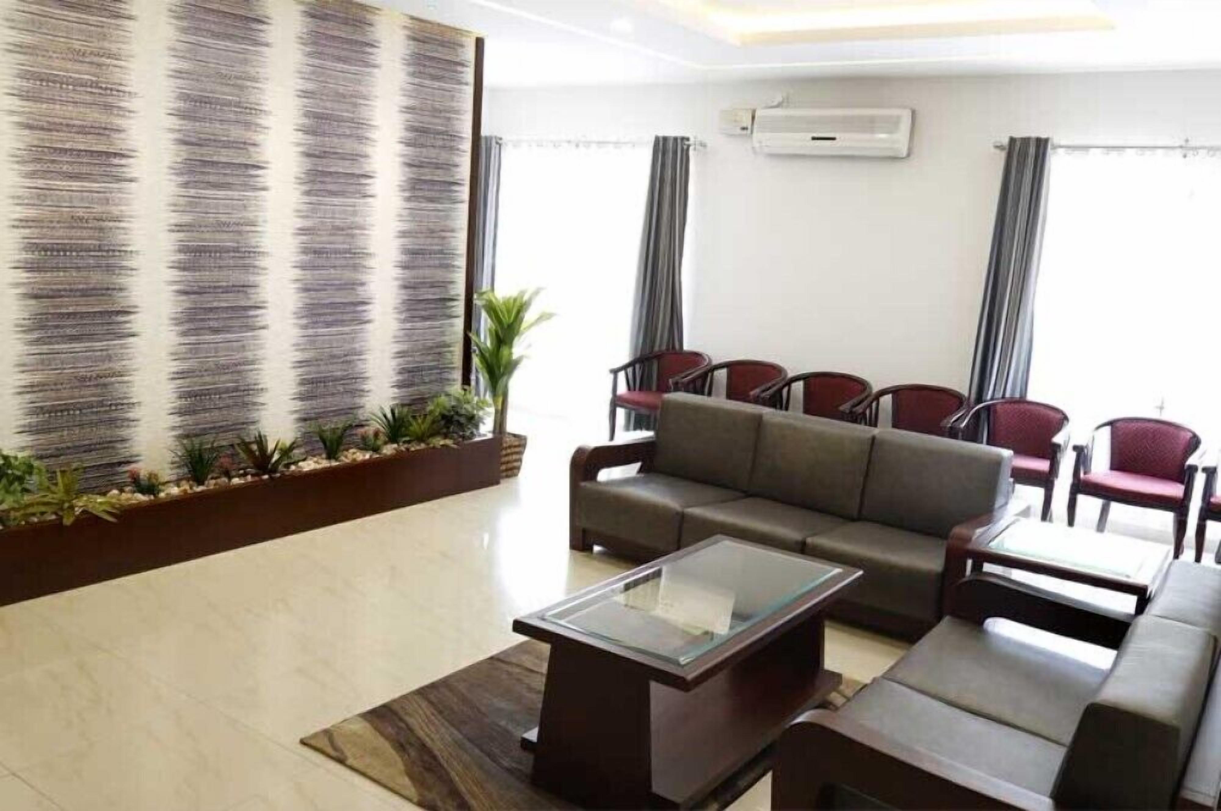Um lobby moderno com um sofá, cadeiras, uma mesa de centro de vidro e um detalhe decorativo na parede.