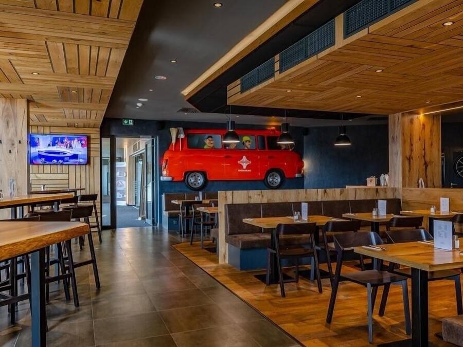 Restaurante com painéis de madeira no teto, decoração com um carro antigo vermelho e várias áreas de estar.