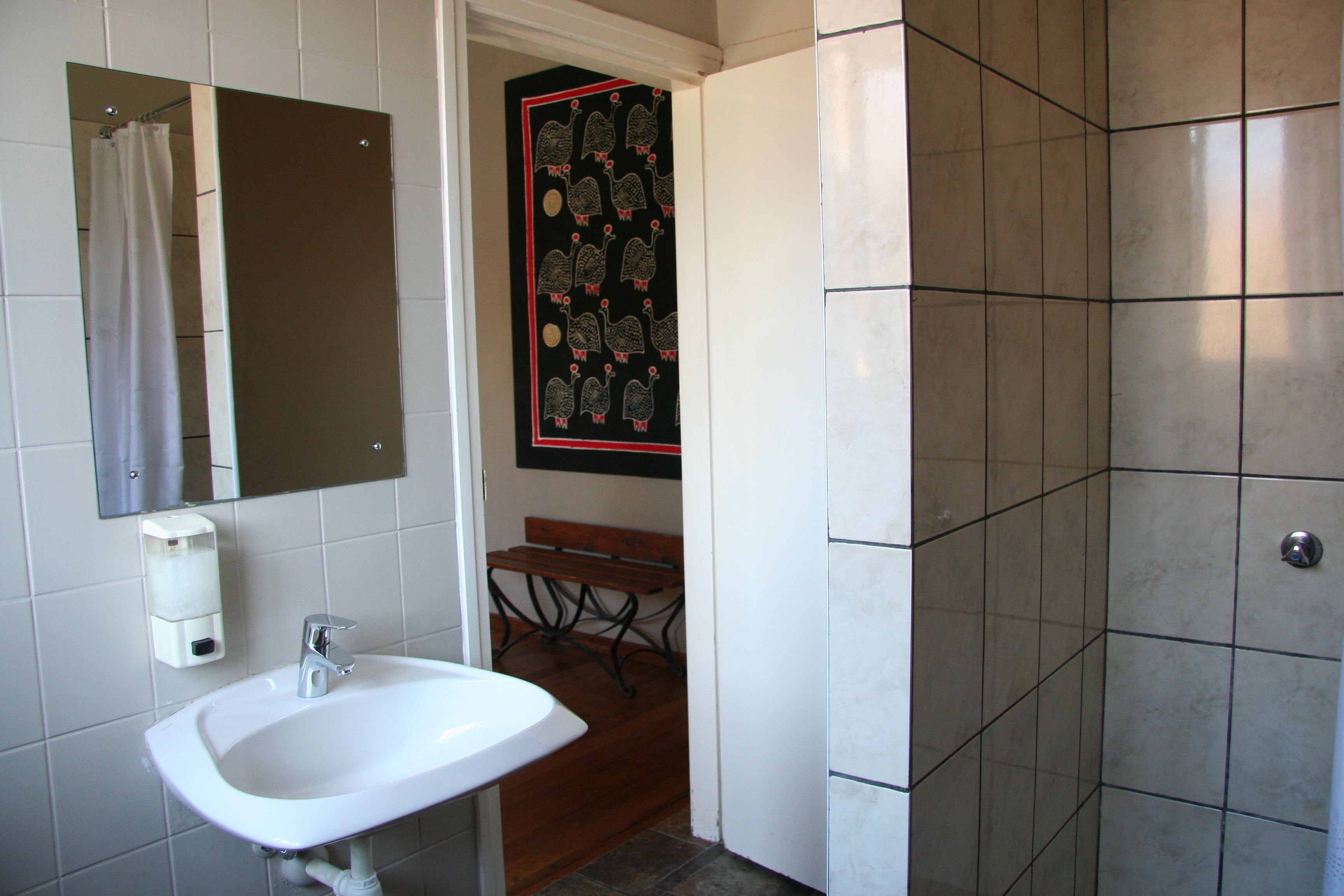 Um banheiro com pia branca, espelho, cortina de chuveiro e box revestido com azulejos.
