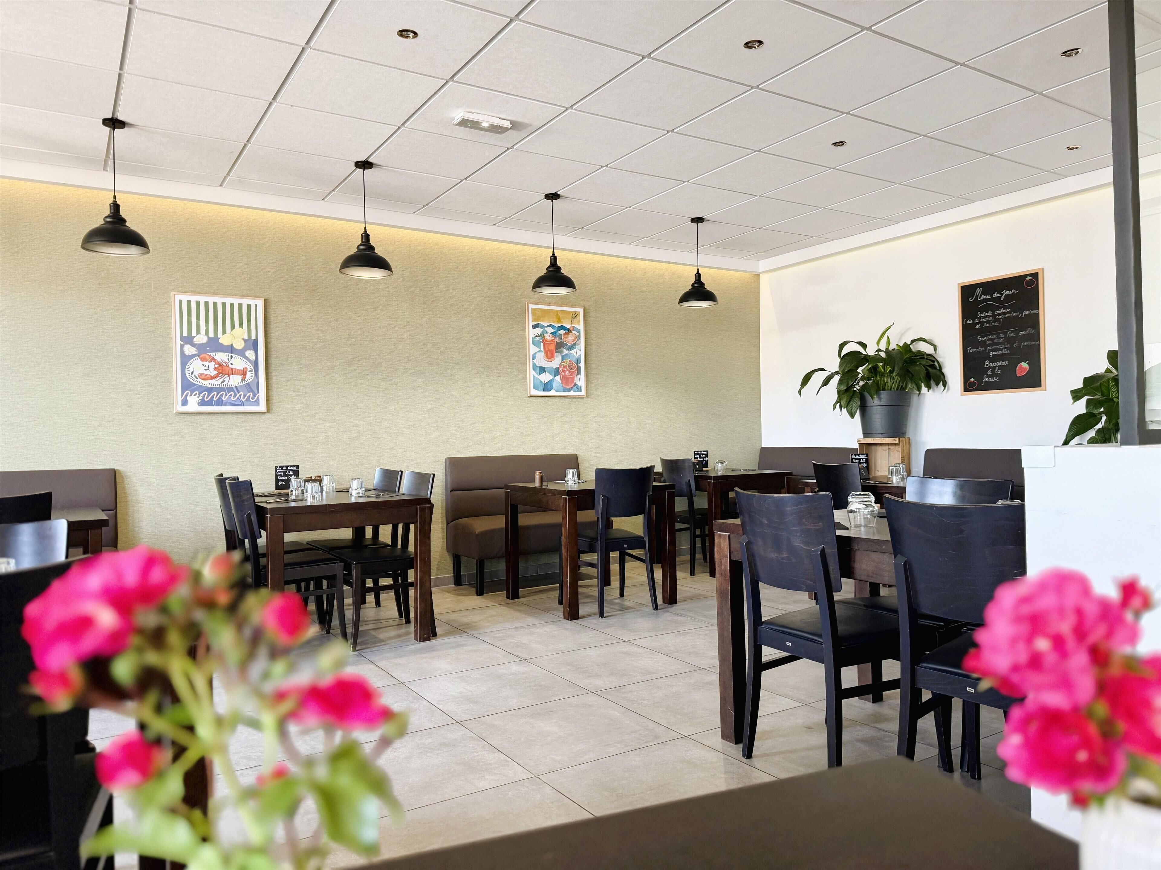 Interior de restaurante com mesas, cadeiras, luminárias pendentes e obras de arte nas paredes.