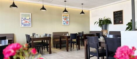 Interior de restaurante com mesas, cadeiras, luminárias pendentes e obras de arte nas paredes.