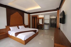 Quarto de hotel com uma cama grande, uma escrivaninha, uma televisão e uma cozinha compacta.