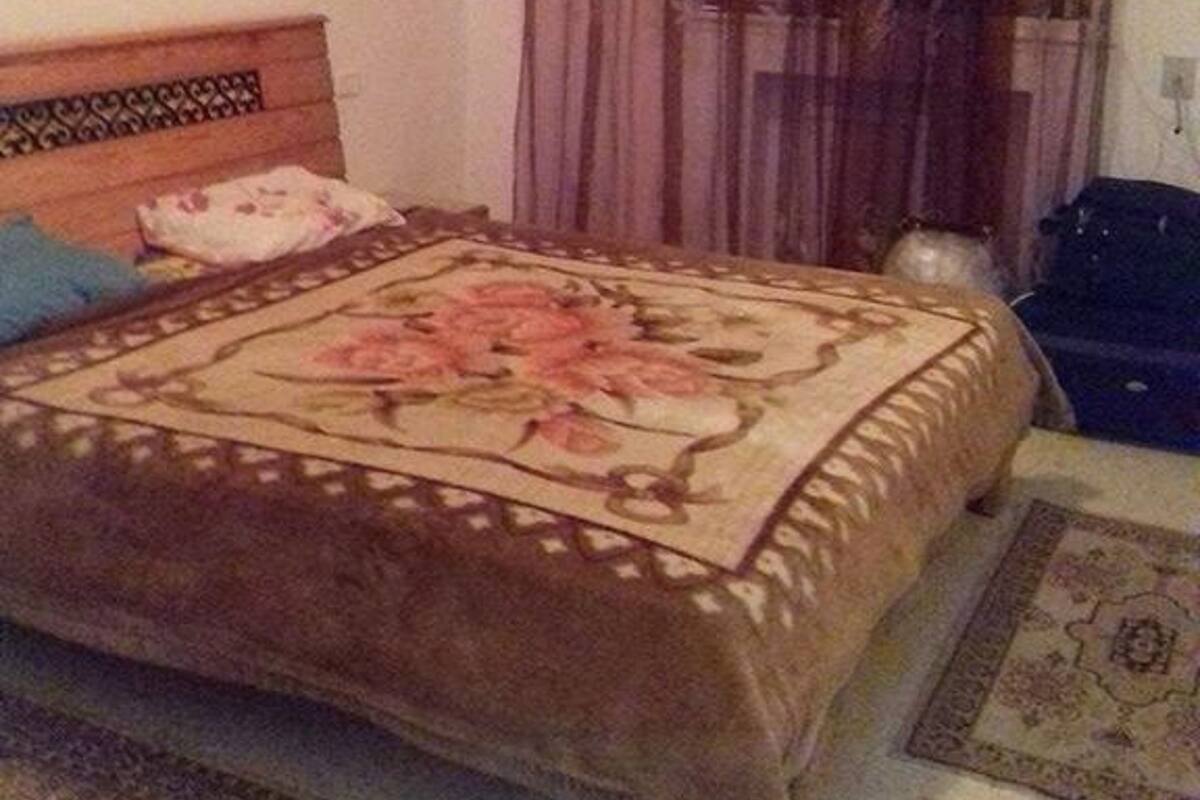 Quarto com cama, mesa de cabeceira, janela com cortinas e mala.