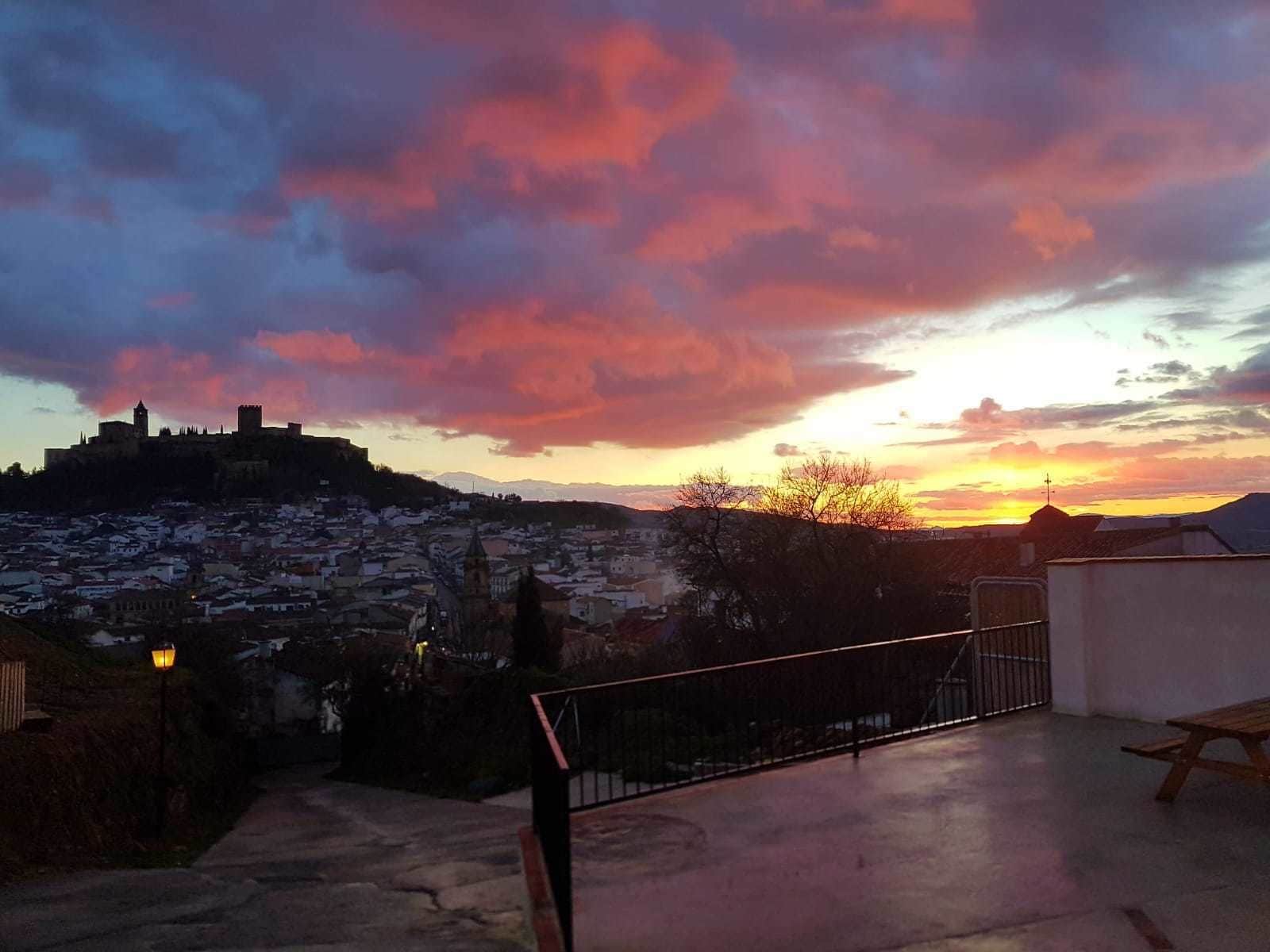 Vista do pôr do sol a partir de uma varanda com vista para uma cidade e uma construção semelhante a um castelo no topo de uma colina.