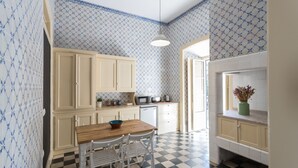 Uma cozinha com piso xadrez, armários brancos, uma mesa de madeira e um lustre.