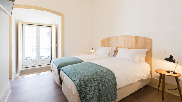Quarto com cama grande, duas mesas de cabeceira, janela com vista e cabeceira de madeira.