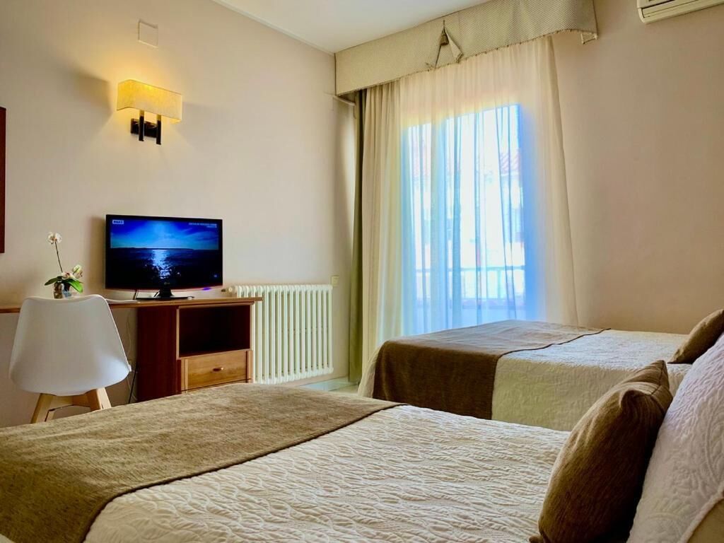 Quarto de hotel com duas camas, televisão, escrivaninha e abajur.