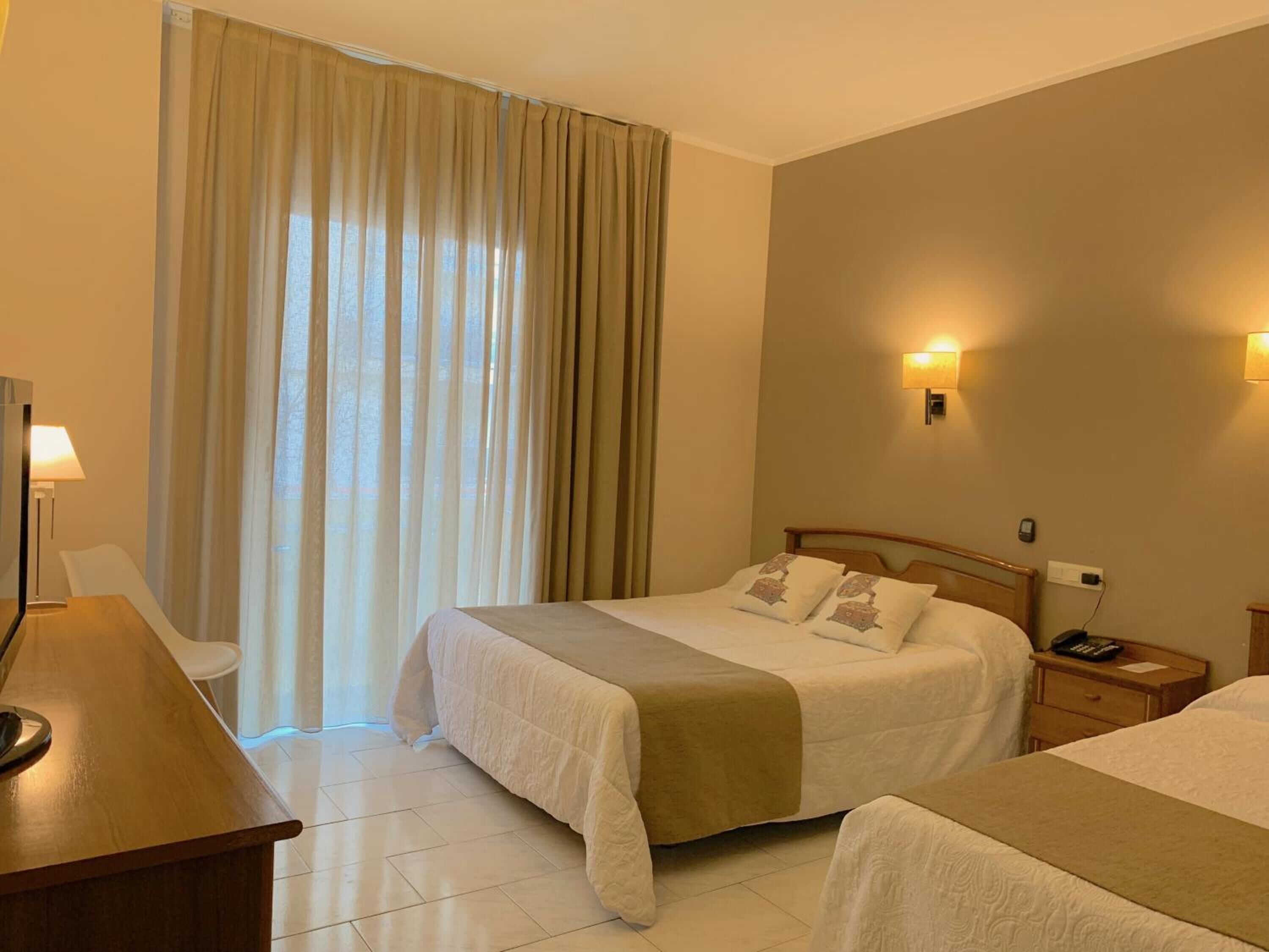 Quarto de hotel com duas camas, uma escrivaninha e uma cadeira.