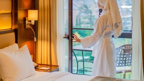 Quarto de hotel com uma cama, mesa de cabeceira, luminária, janela com cortinas e vista para a cidade.