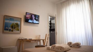 Quarto de hotel com cama, escrivaninha, cadeira, televisão e janela com cortinas.