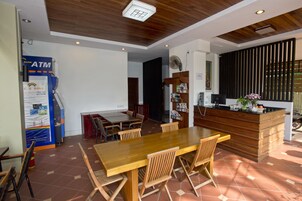 Um restaurante com mesa e cadeiras de madeira, um balcão com uma planta e um caixa eletrônico à esquerda.
