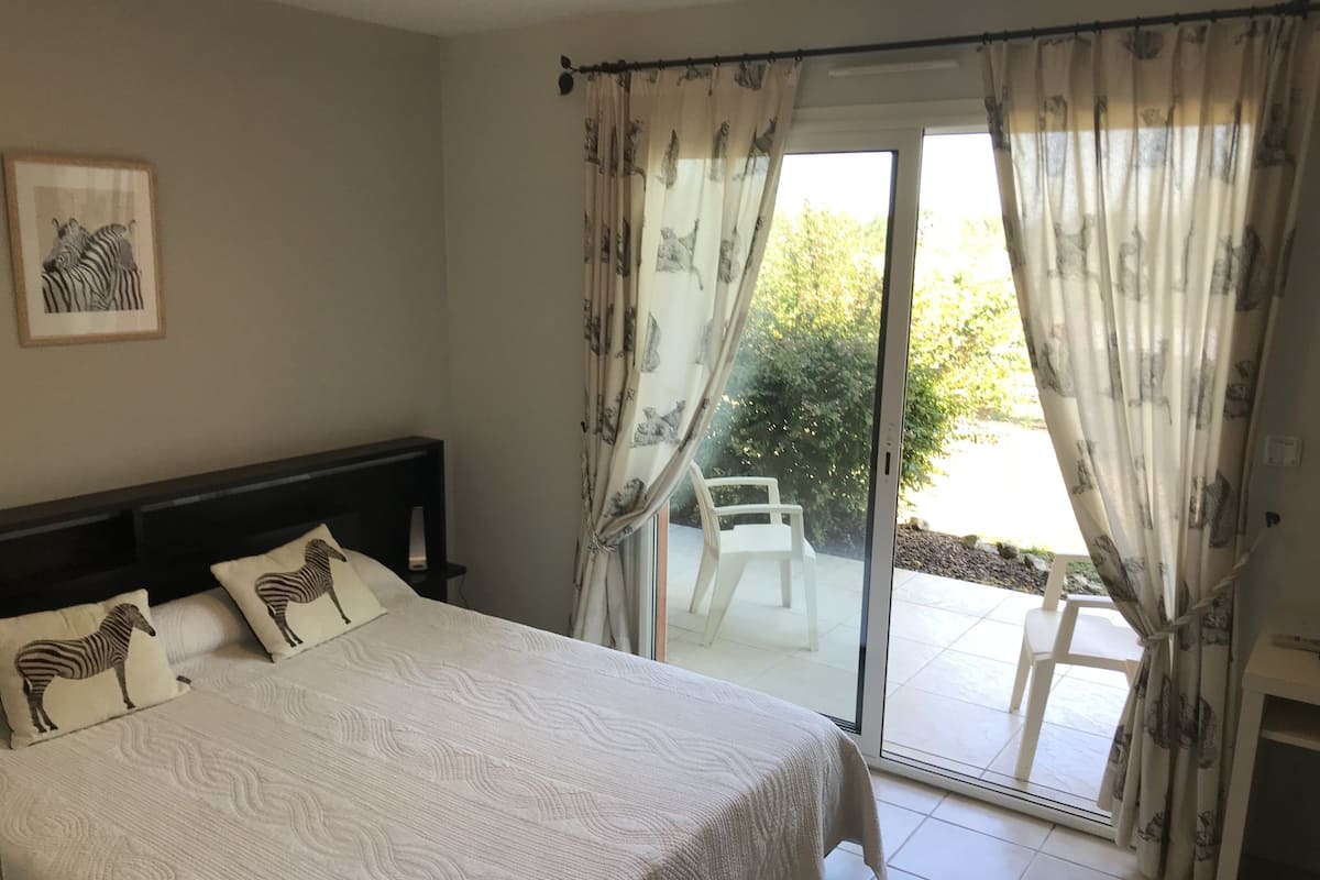 Quarto com cama, almofadas com tema de zebra, um quadro na parede e uma porta de correr de vidro que dá para uma área externa com uma cadeira.