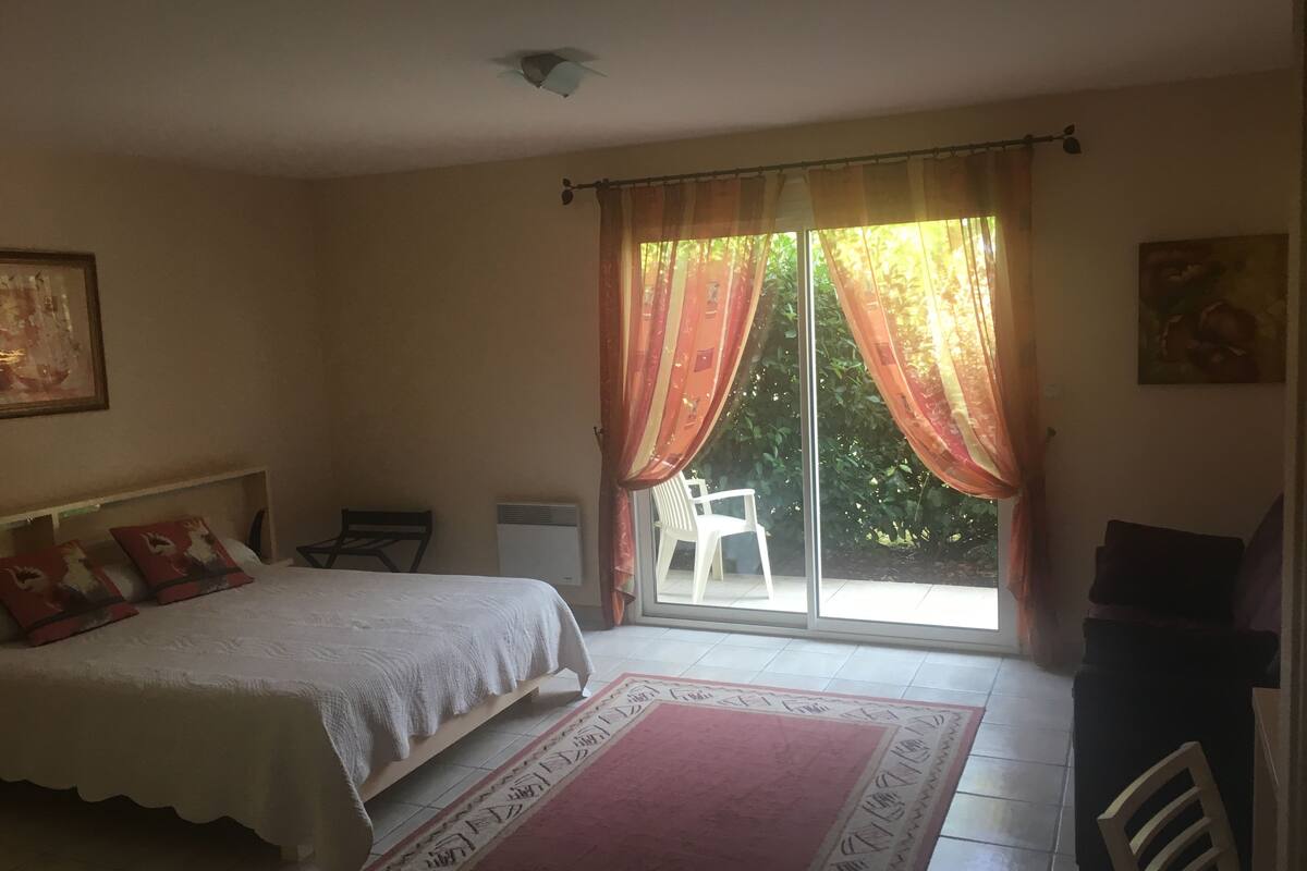 Quarto com uma cama, uma cadeira, uma escrivaninha e uma janela com cortinas.