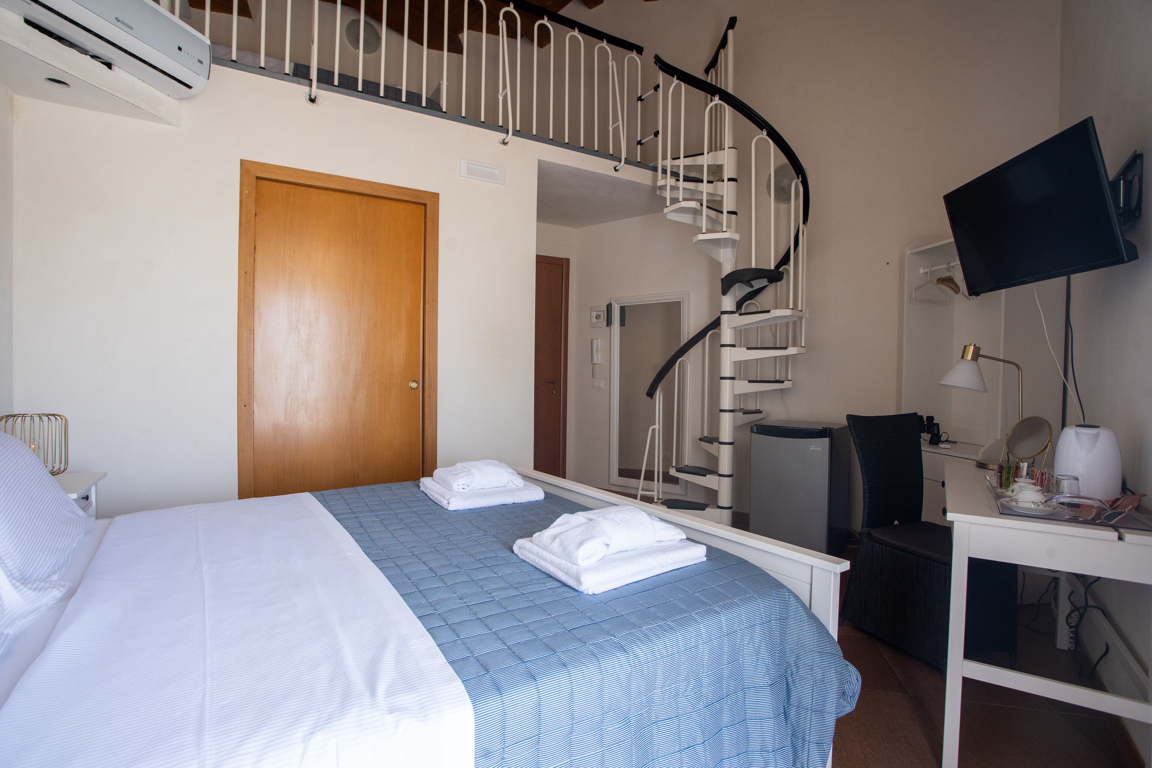 Quarto de hotel com cama, escrivaninha, cadeira, televisão e escada.