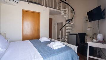 Quarto de hotel com cama, escrivaninha, cadeira, televisão e escada.