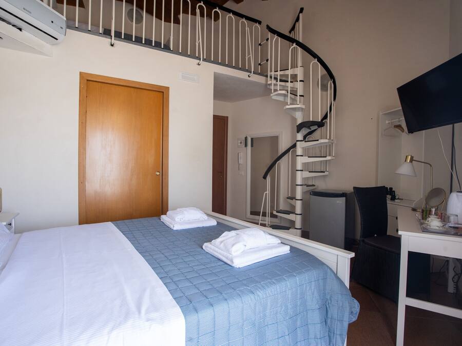 Quarto de hotel com cama, escrivaninha, cadeira, televisão e escada.