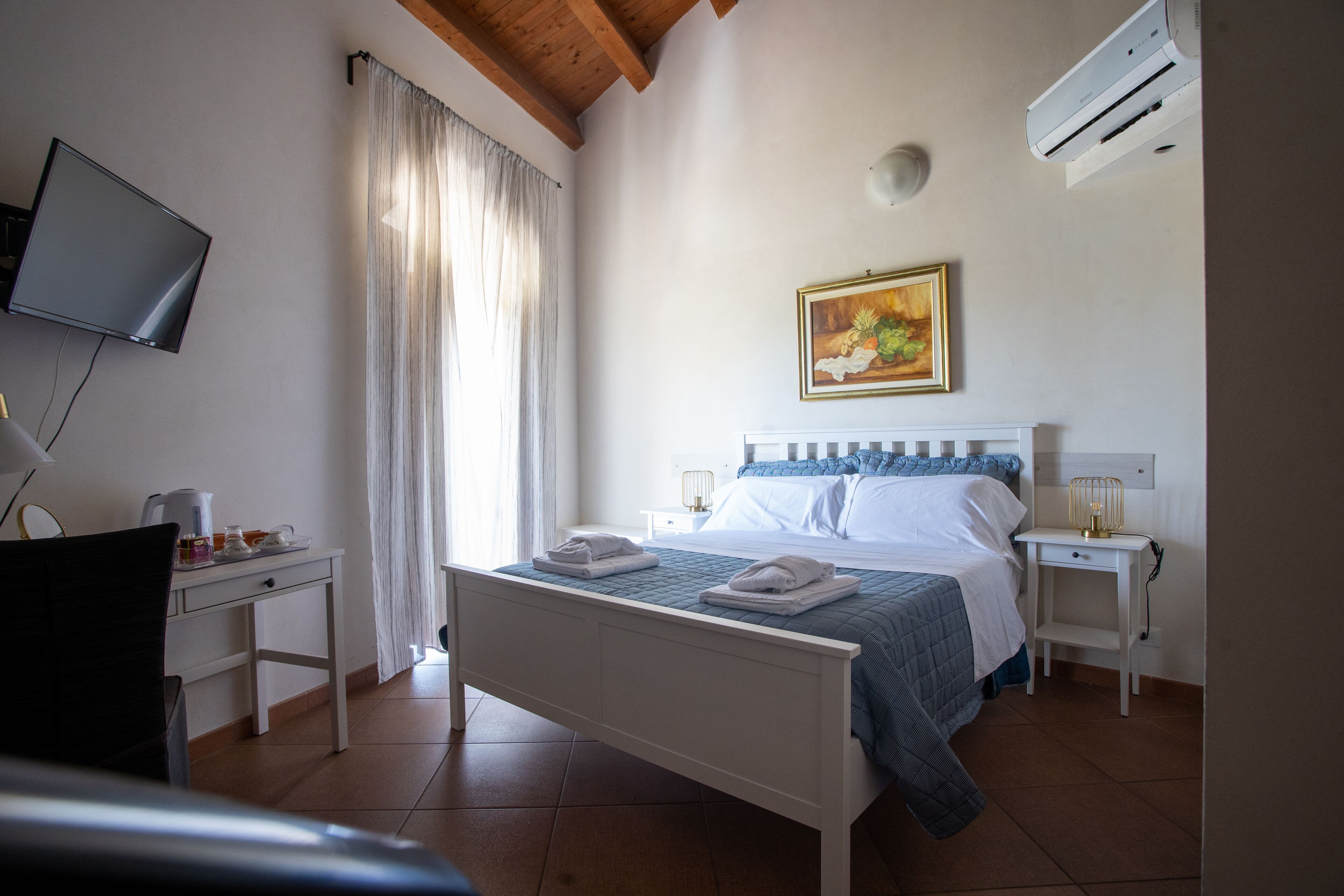 Um quarto com cama, escrivaninha, cadeira, televisão, quadro e ar condicionado.