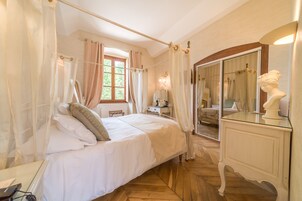 Quarto com cama de dossel, penteadeira com espelho e busto de escultura no criado-mudo.