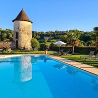Piscina com espreguiçadeiras e uma torre de pedra.