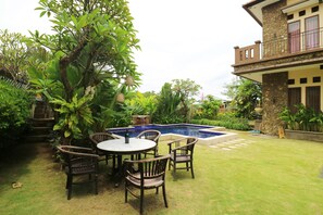 Um quintal com piscina, mesa de jantar e cadeiras, e vegetação exuberante.