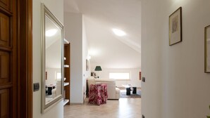 Corredor que dá para uma sala de estar com sofá, mesa e abajur.