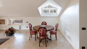 Uma sala de jantar com uma mesa redonda e seis cadeiras, um arranjo de flores e um claraboia com vista para edifícios.