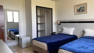 Quarto de hotel com duas camas, um guarda-roupa, uma escrivaninha e um espelho.
