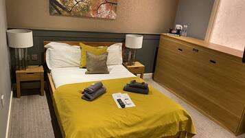 Quarto de hotel com cama, duas mesas de cabeceira, cómoda de madeira e um quadro na parede.