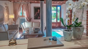 Quarto aconchegante com sofá, mesa de centro e abajur. Há duas orquídeas em vasos e um chaveiro sobre a mesa.