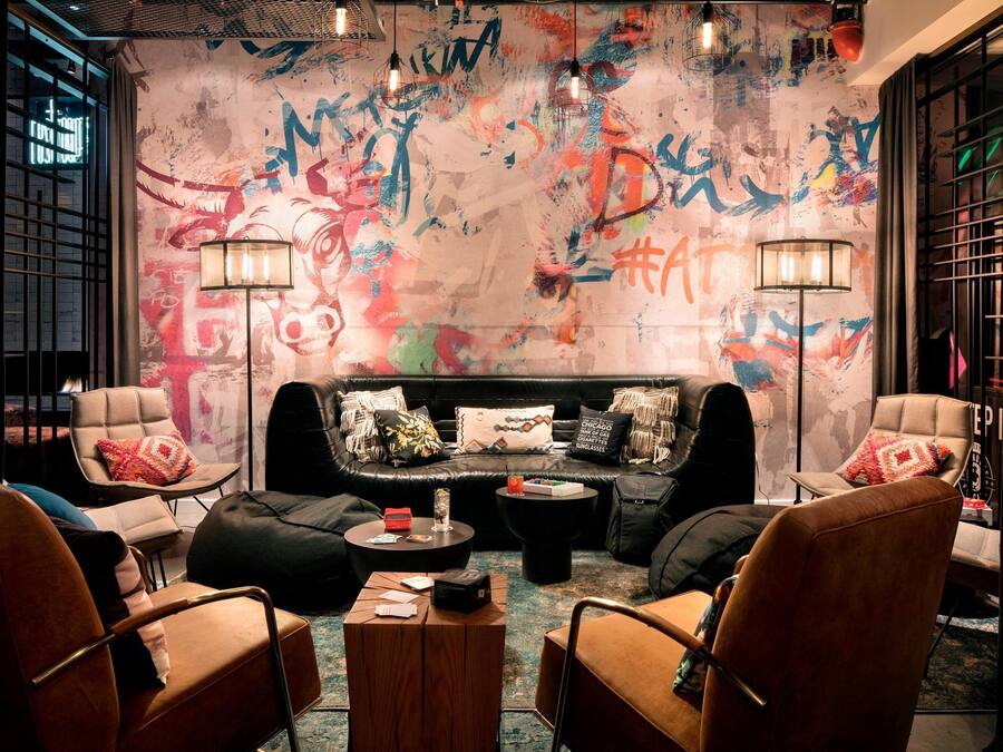 Um lounge moderno com um sofá de couro preto, poltronas e uma mesa de centro. As paredes são decoradas com arte abstrata e grafites.