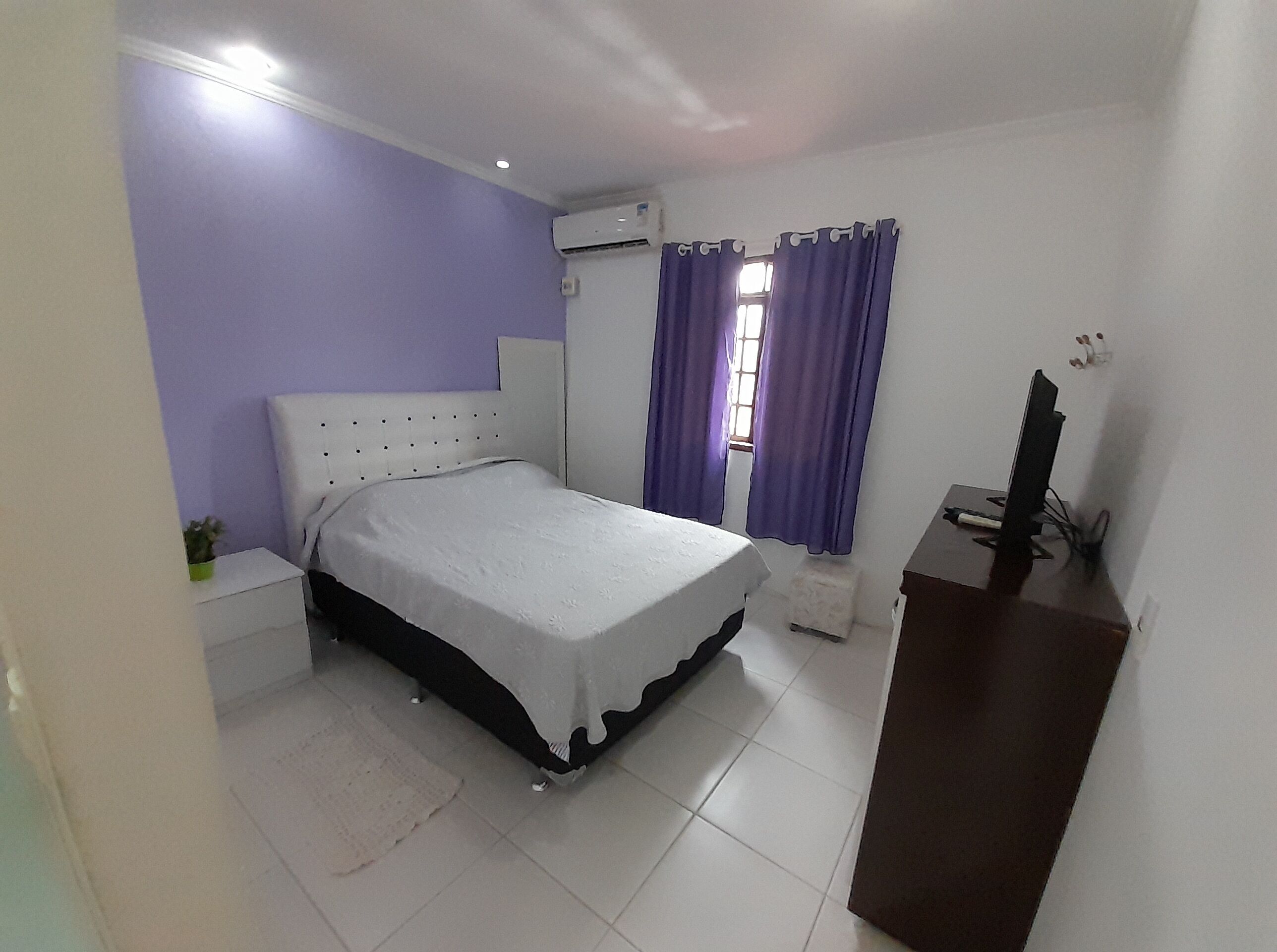 Quarto com cama, escrivaninha, ar-condicionado e cortinas roxas.