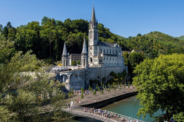 Uma igreja histórica com uma torre imponente, localizada à beira de um rio com uma ponte para pedestres.