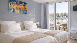 Quarto de hotel com duas camas, uma janela grande com vista e um quadro colorido na parede.