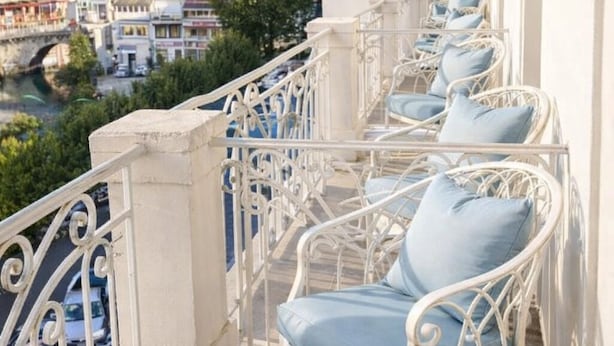 Varanda com cadeiras de vime branco e vista para um rio e edifícios.