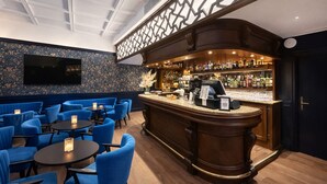 Uma área de bar com balcão de madeira, cadeiras estofadas azuis e parede com padrão.
