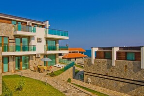 Um edifício moderno de vários andares com varandas, fachada de pedra e vista clara para o mar.