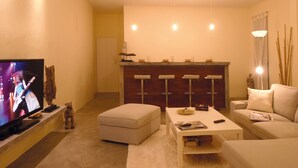 Uma sala moderna com televisão de tela plana, sofá, mesa de centro e área de cozinha com banquetas.