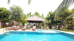 Uma piscina com espreguiçadeiras e um gazebo cercado por palmeiras e vegetação.