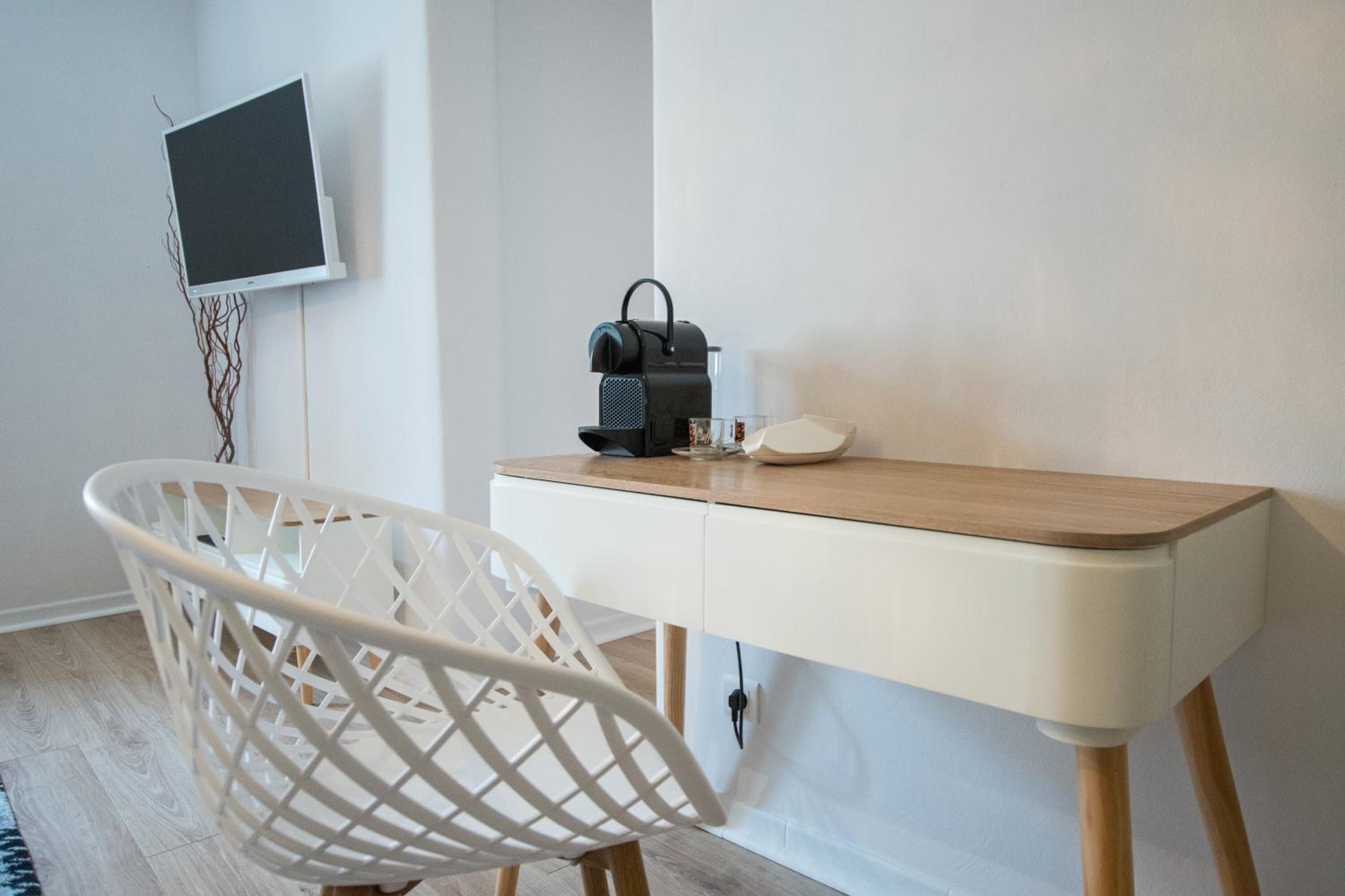 Quarto moderno com uma cadeira branca, uma escrivaninha de madeira, uma TV de tela plana e uma máquina de café.