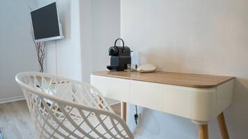 Quarto moderno com uma cadeira branca, uma escrivaninha de madeira, uma TV de tela plana e uma máquina de café.
